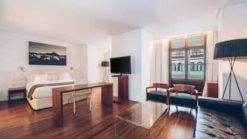 Quarto de hotel moderno com cama, televisão, mesa de centro de vidro, sofá e área de jantar.