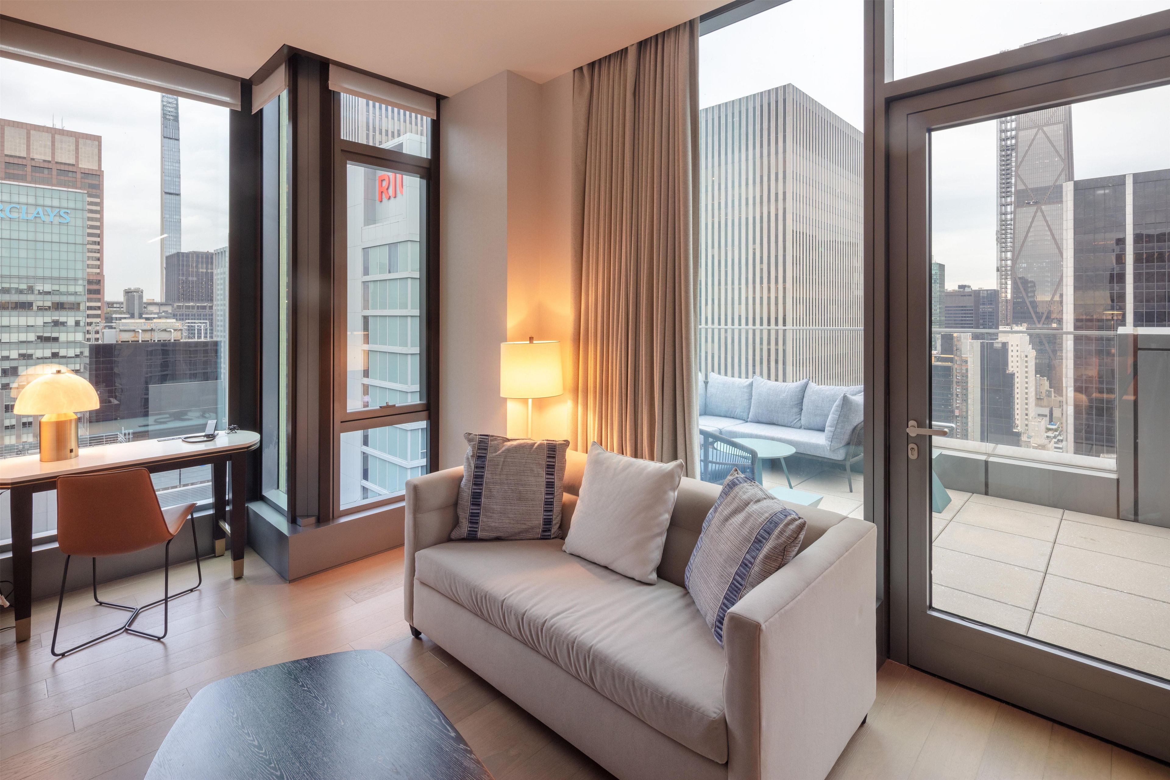 Quarto de hotel moderno com sofá, escrivaninha e vista para a paisagem urbana.