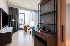 Quarto de hotel moderno com uma janela ampla, televisão de tela plana, sofá, mesa de centro e minibar.