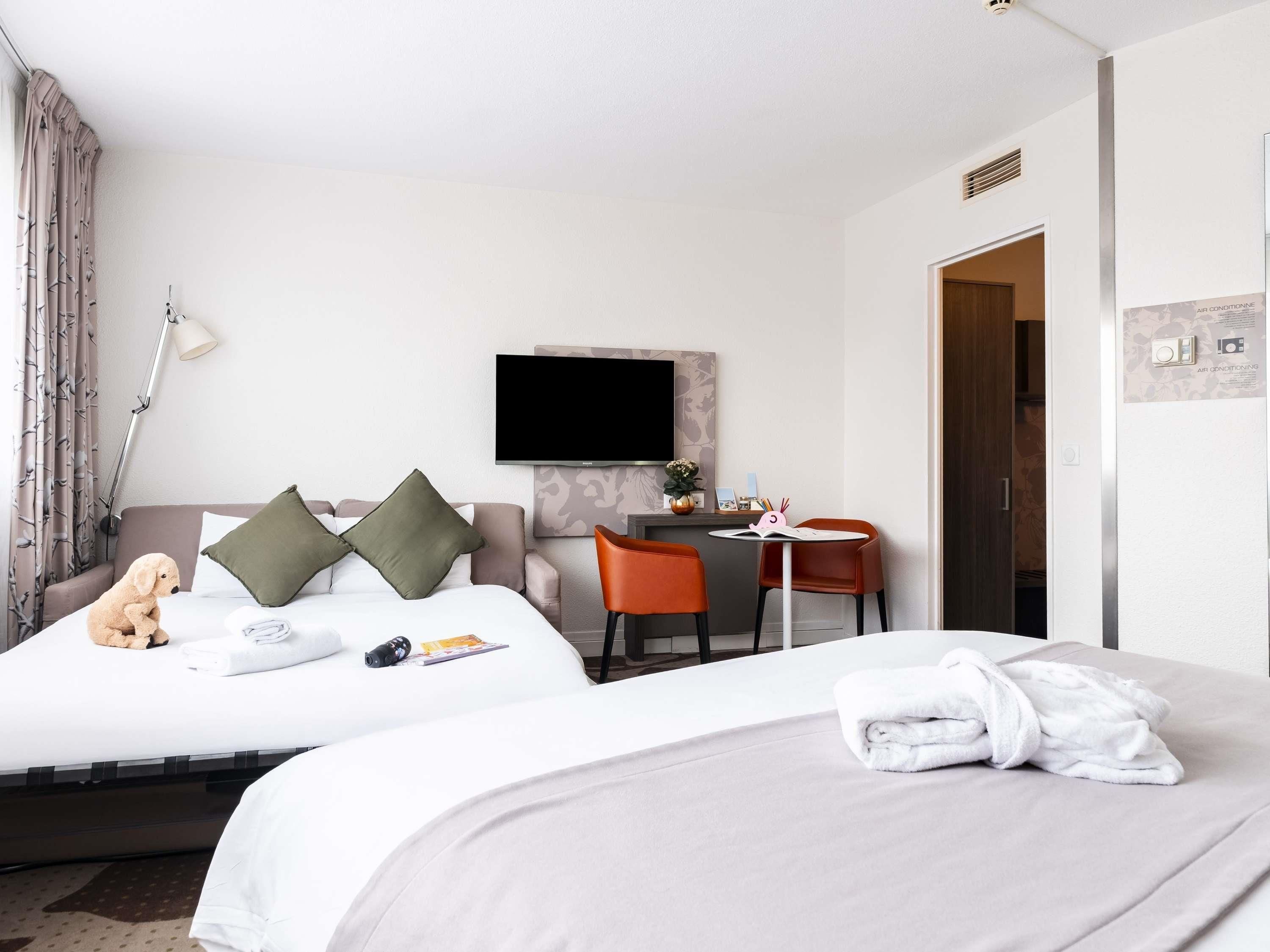 Quarto de hotel com cama, escrivaninha, cadeira, televisão e porta.