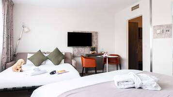 Quarto de hotel com cama, escrivaninha, cadeira, televisão e porta.