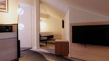 Quarto de hotel moderno com uma televisão de tela plana grande, um sofá, uma pequena mesa lateral de madeira e um tapete estampado.