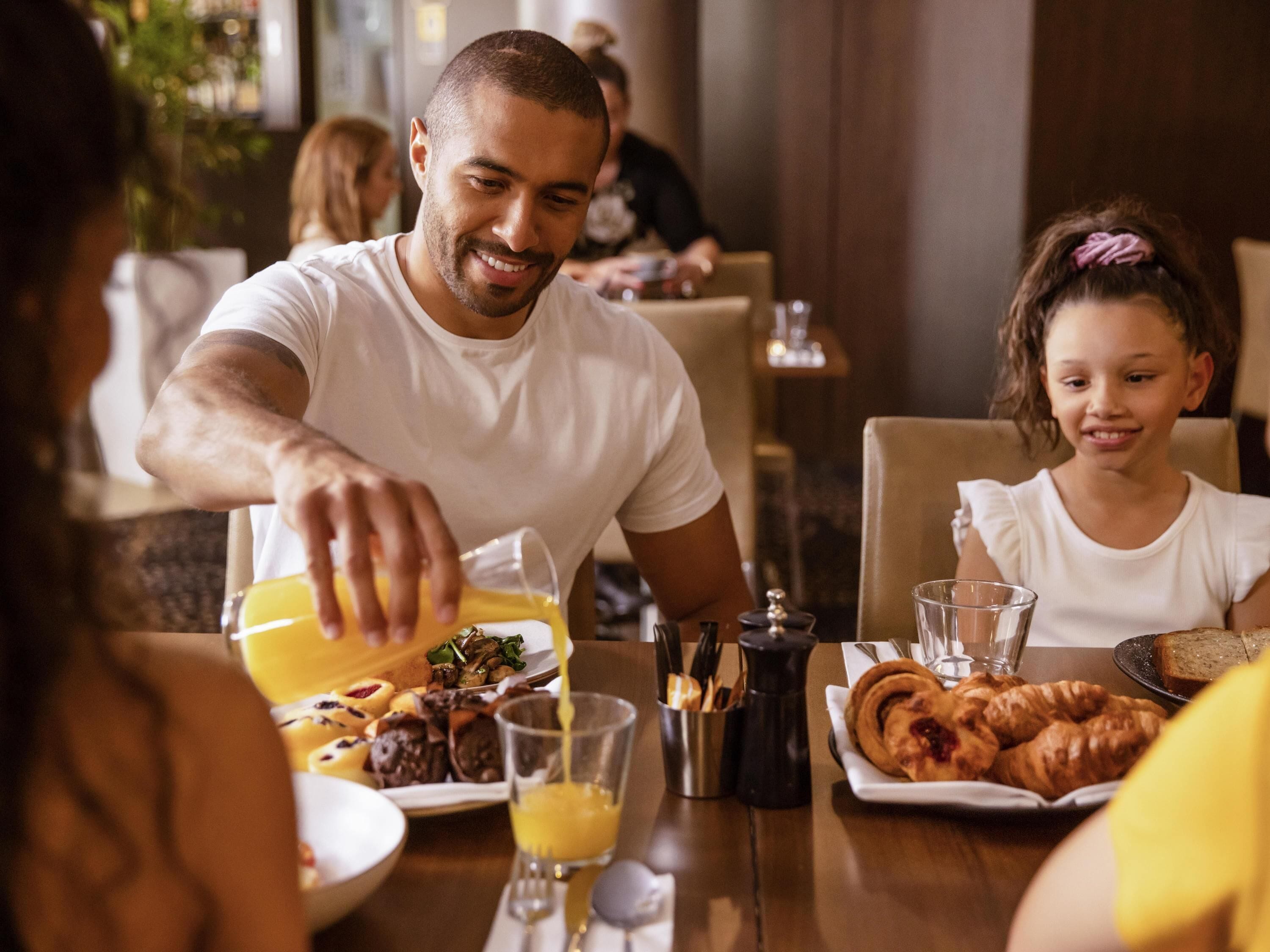 Mesa de jantar com diversos pratos, incluindo croissants e um copo de suco de laranja.