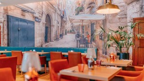 Restaurante com um mural retratando uma cena de rua, mesas e cadeiras de madeira e um lustre pendurado.