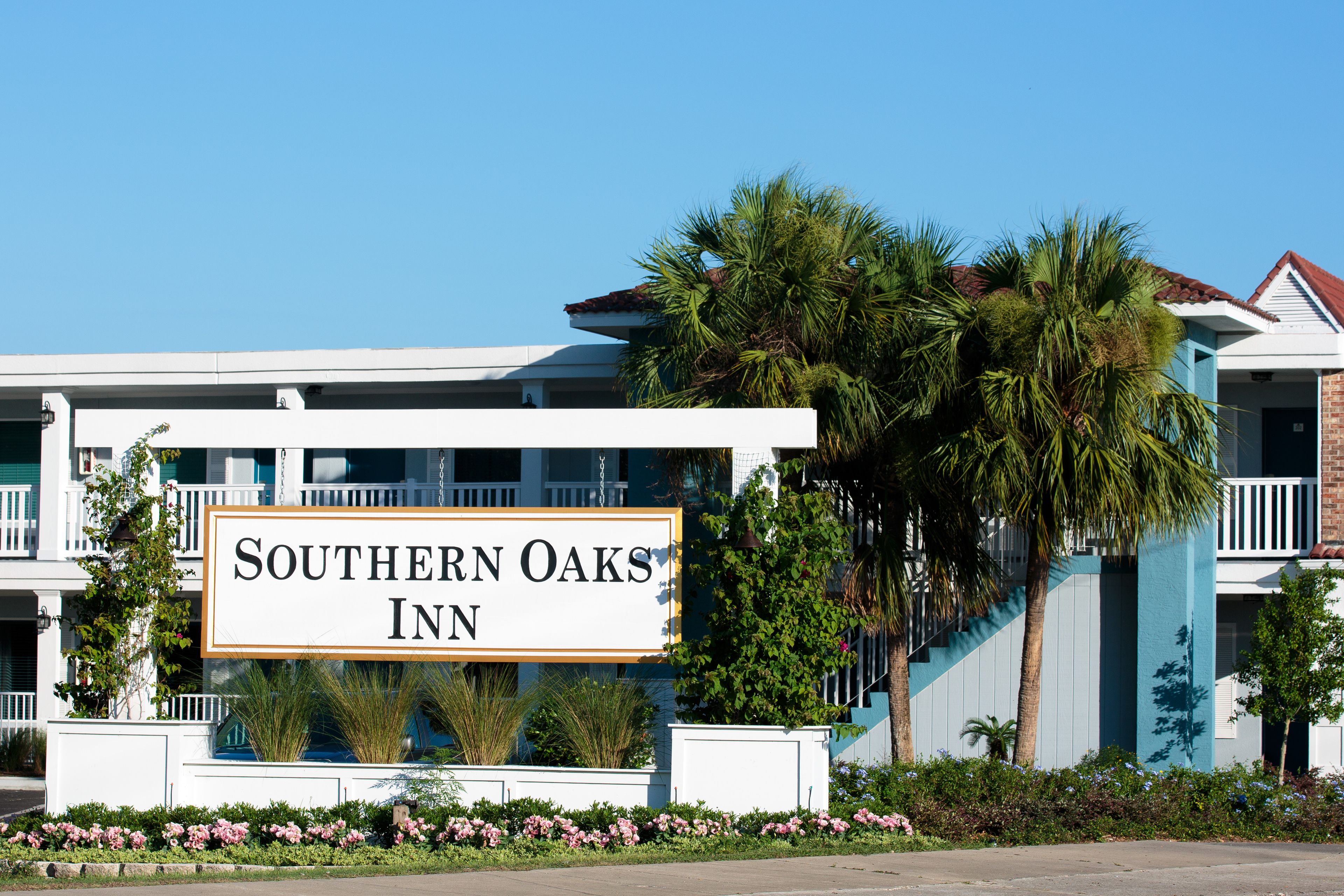 Placa de hotel com o nome 'Southern Oaks Inn' e um edifício com fachada branca e detalhes azuis.