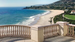 Vista costeira de uma varanda com guarda-corpo curvo, com vista para uma praia arenosa e oceano.