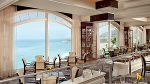 Uma área de jantar luxuosa com vista para o oceano, mobiliário elegante e uma escadaria imponente.