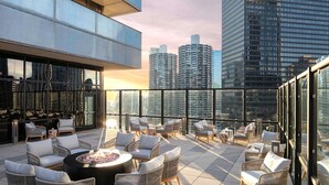Terraço no terraço com área de estar ao ar livre e lareira, com vista para um horizonte urbano com edifícios altos.