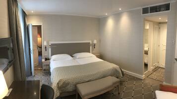 Quarto de hotel com cama, mesa de cabeceira, luminária e um banco.