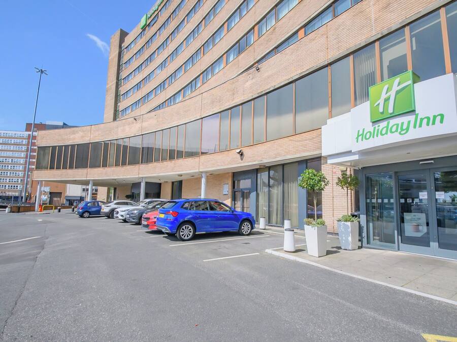 Um hotel Holiday Inn com um estacionamento e vários carros estacionados na frente.