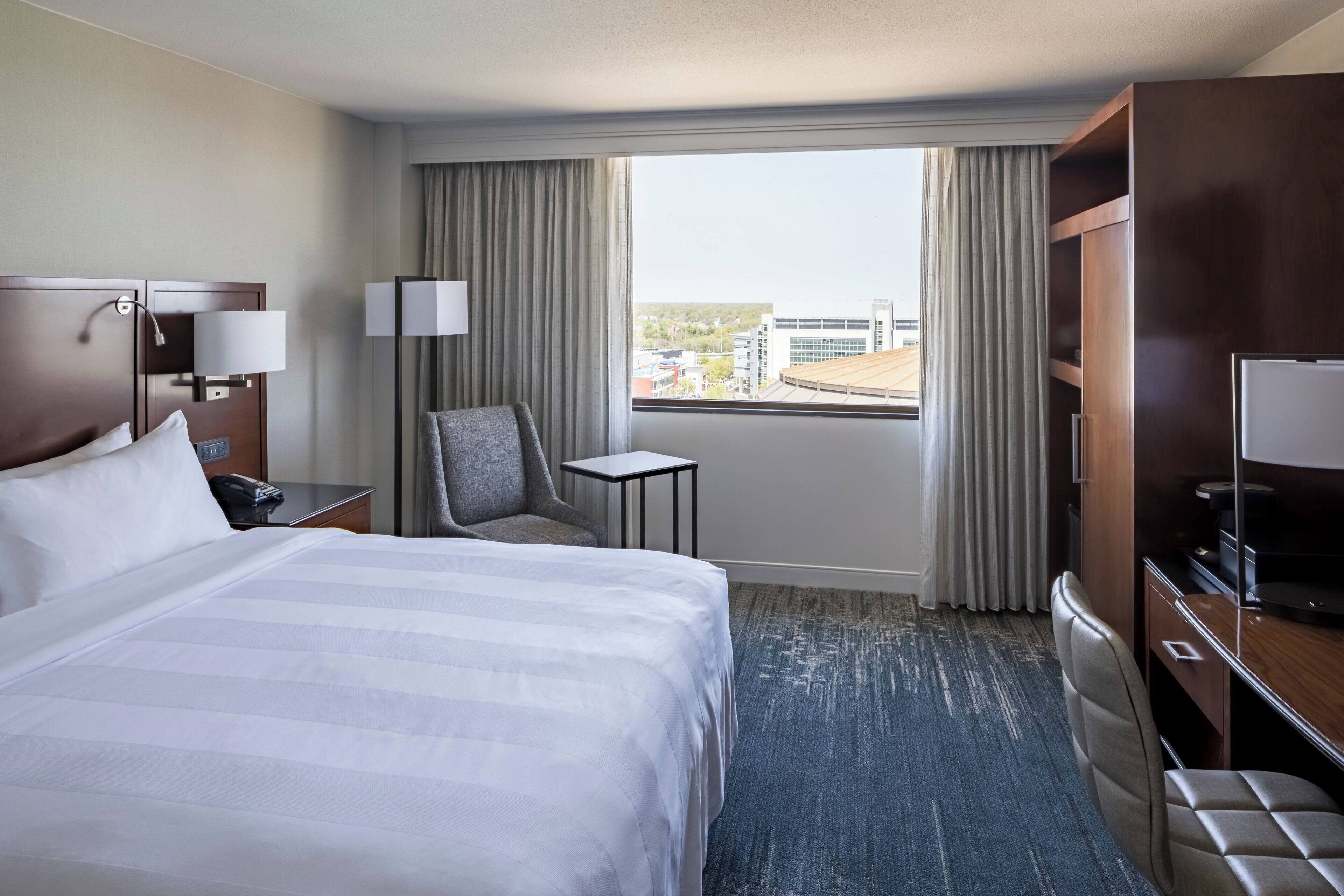 Quarto de hotel com uma cama grande, uma escrivaninha, uma cadeira, uma televisão e vista para a cidade.