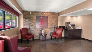 Um saguão de hotel com parede de pedra, duas poltronas de couro vermelho, uma máquina de café e uma placa com a inscrição 'Red Roof Inn'.