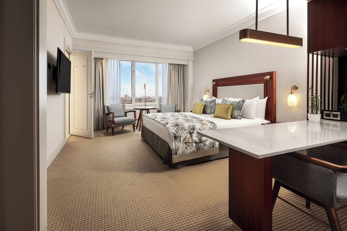 Quarto de hotel com cama, secretária, cadeira, televisão e vista para a cidade.