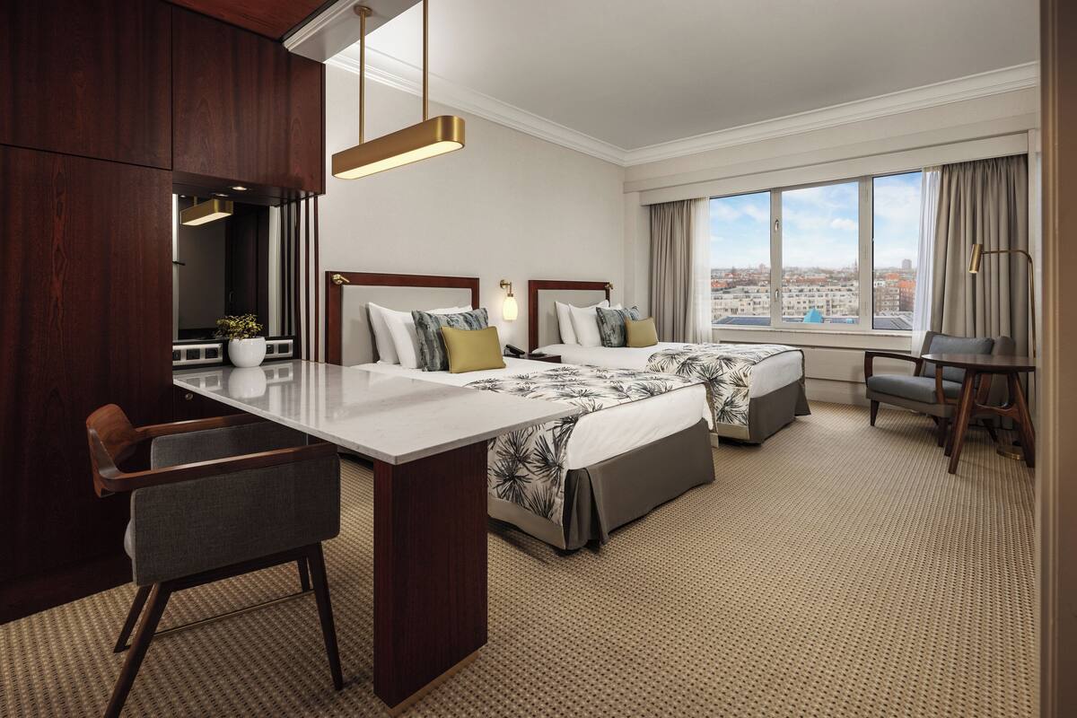 Quarto de hotel com uma cama grande, uma mesa e uma cadeira. Tem uma janela com vista para a cidade.
