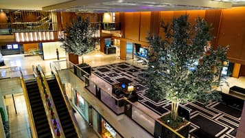 Um saguão de hotel com vários níveis, escadas rolantes, balcões de recepção e plantas dentro de casa.