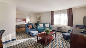 Quarto de hotel com cama, sofá azul, mesa de centro, escrivaninha e janela com cortinas.