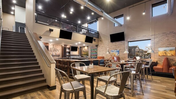 Um restaurante moderno com escada, várias mesas e cadeiras.