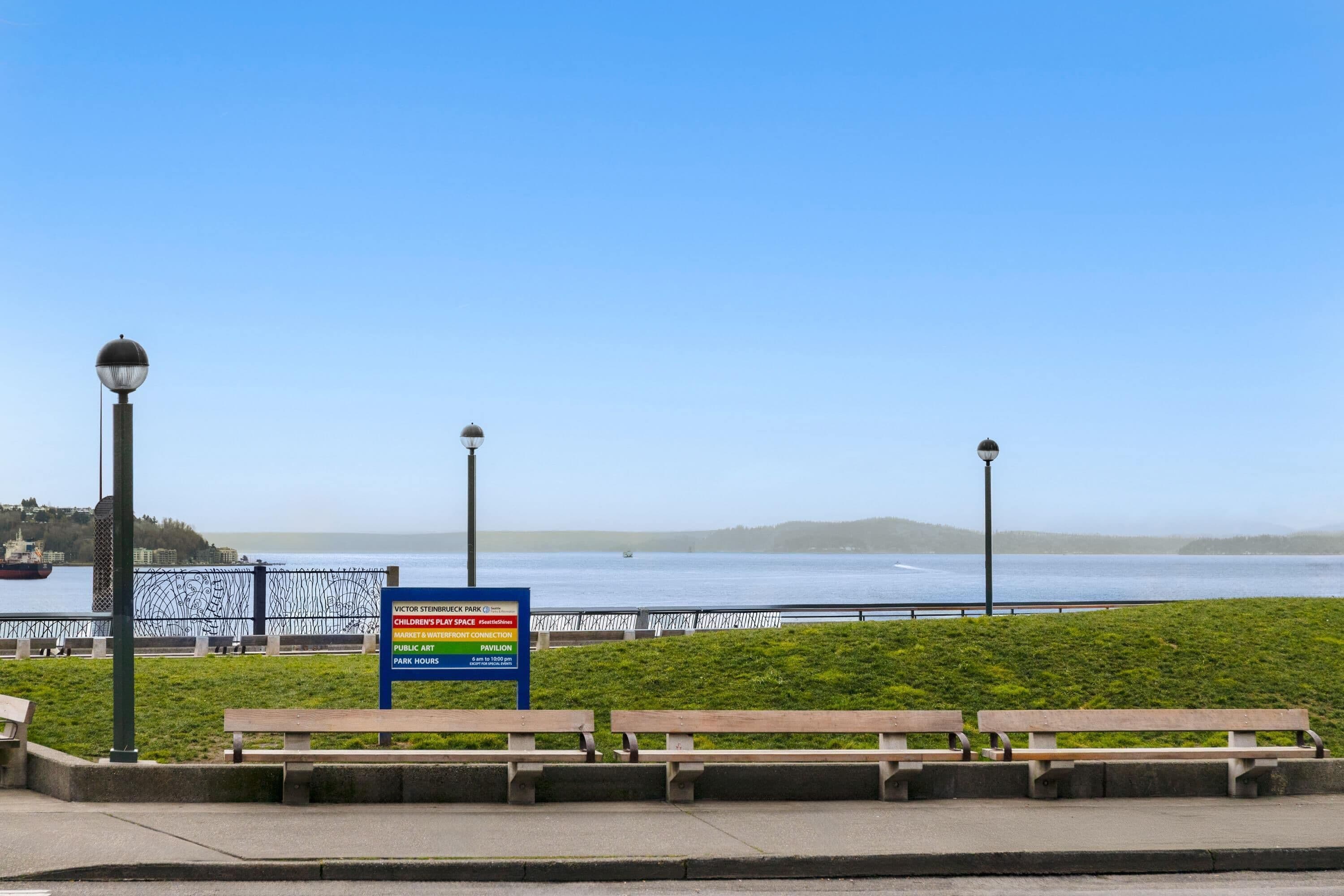 Um parque à beira-mar com bancos, uma placa informativa e vista para a água.