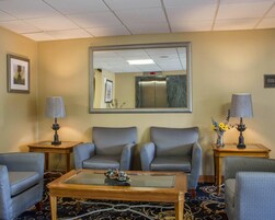 Quarto de hotel com duas poltronas, uma mesa de centro, duas luminárias, um espelho e um quadro na parede.