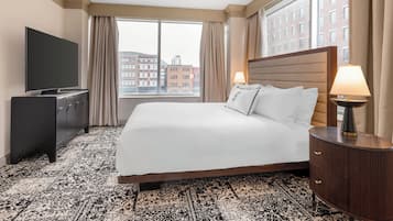 Quarto de hotel com uma cama grande, televisão, cômoda e janela com vista para a cidade.