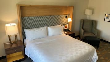 Quarto de hotel com cama grande, mesa de cabeceira com abajur, cadeira e telefone fixado na parede.