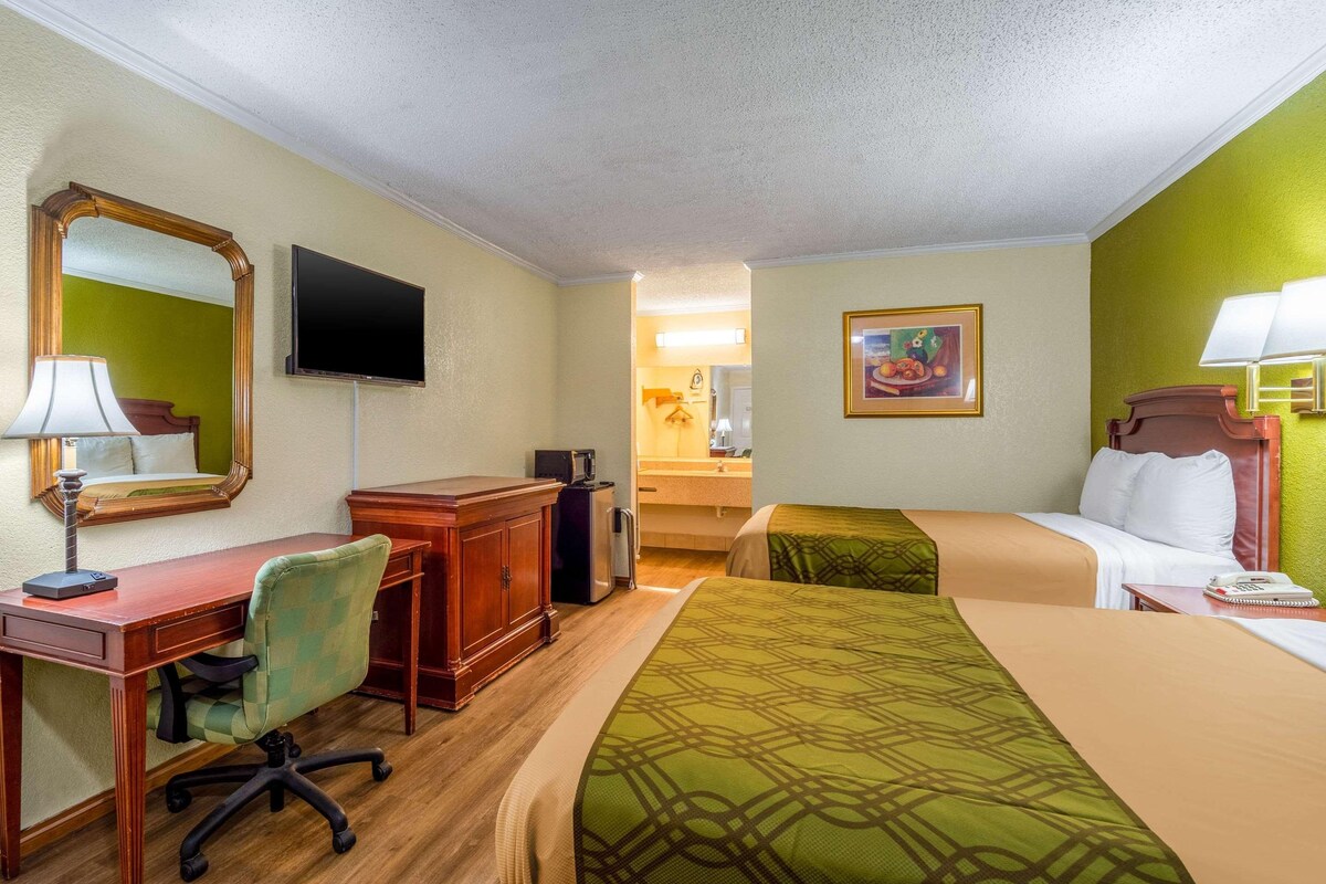 Quarto de hotel com escrivaninha, cadeira, cama, televisão e um quadro na parede.