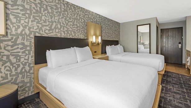 Quarto de hotel com duas camas, parede estampada, um espelho e uma porta.
