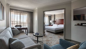 Quarto de hotel com sofá, uma cadeira, mesa pequena, cama e televisão.