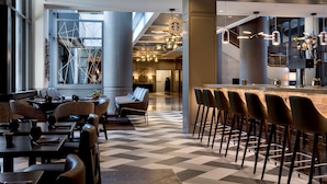 Um hall de hotel moderno com piso xadrez, áreas de estar, um bar e um letreiro da Starbucks.