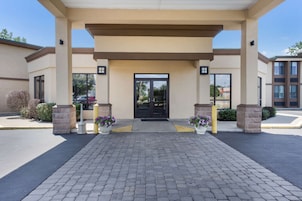 Entrada de hotel com galeria coberta, plantas em vasos e calçada de ladrilhos.