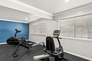 Ginásio com equipamentos de exercício, incluindo uma bicicleta ergométrica e uma esteira, num espaço com paredes azuis e teto branco.