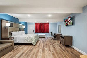Quarto de hotel com cama, escrivaninha, cadeira, televisão e cortina vermelha.