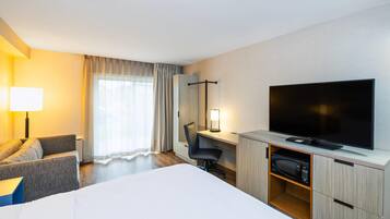 Quarto de hotel com cama, escrivaninha, cadeira, televisão e janela com cortinas.