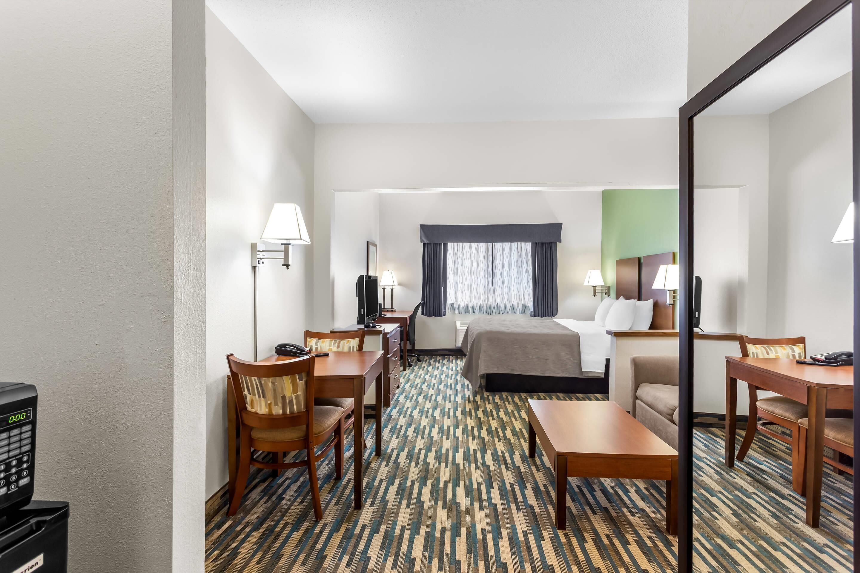 Quarto de hotel com cama, escrivaninha, cadeira, mesa, luminária e espelho.