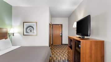 Quarto de hotel com uma cama, uma televisão sobre um armário de madeira, uma obra de arte emoldurada na parede e uma porta que dá para outro quarto.