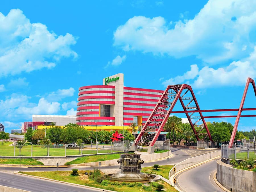 Um hotel Holiday Inn com fachada distinta listrada em vermelho e branco, uma grande estrutura de ponte vermelha e uma fonte em primeiro plano.
