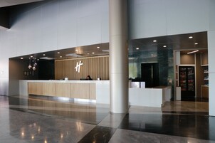 Um lobby moderno de hotel com uma mesa de recepção, um pilar grande e um muro de vidro.