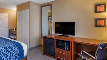 Quarto de hotel com cama, escrivaninha, televisão, micro-ondas e frigorífico.