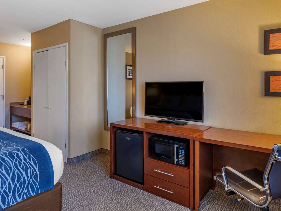 Quarto de hotel com cama, escrivaninha, televisão, micro-ondas e frigorífico.