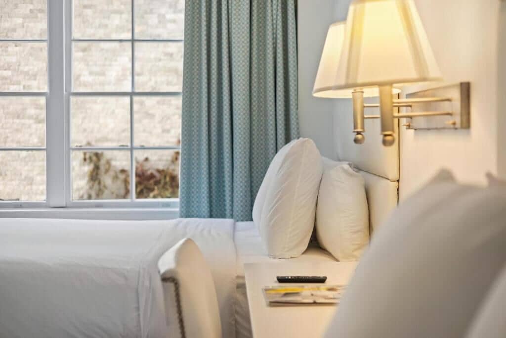 Quarto de hotel com uma cama, mesa de cabeceira com abajur e uma janela com cortinas.