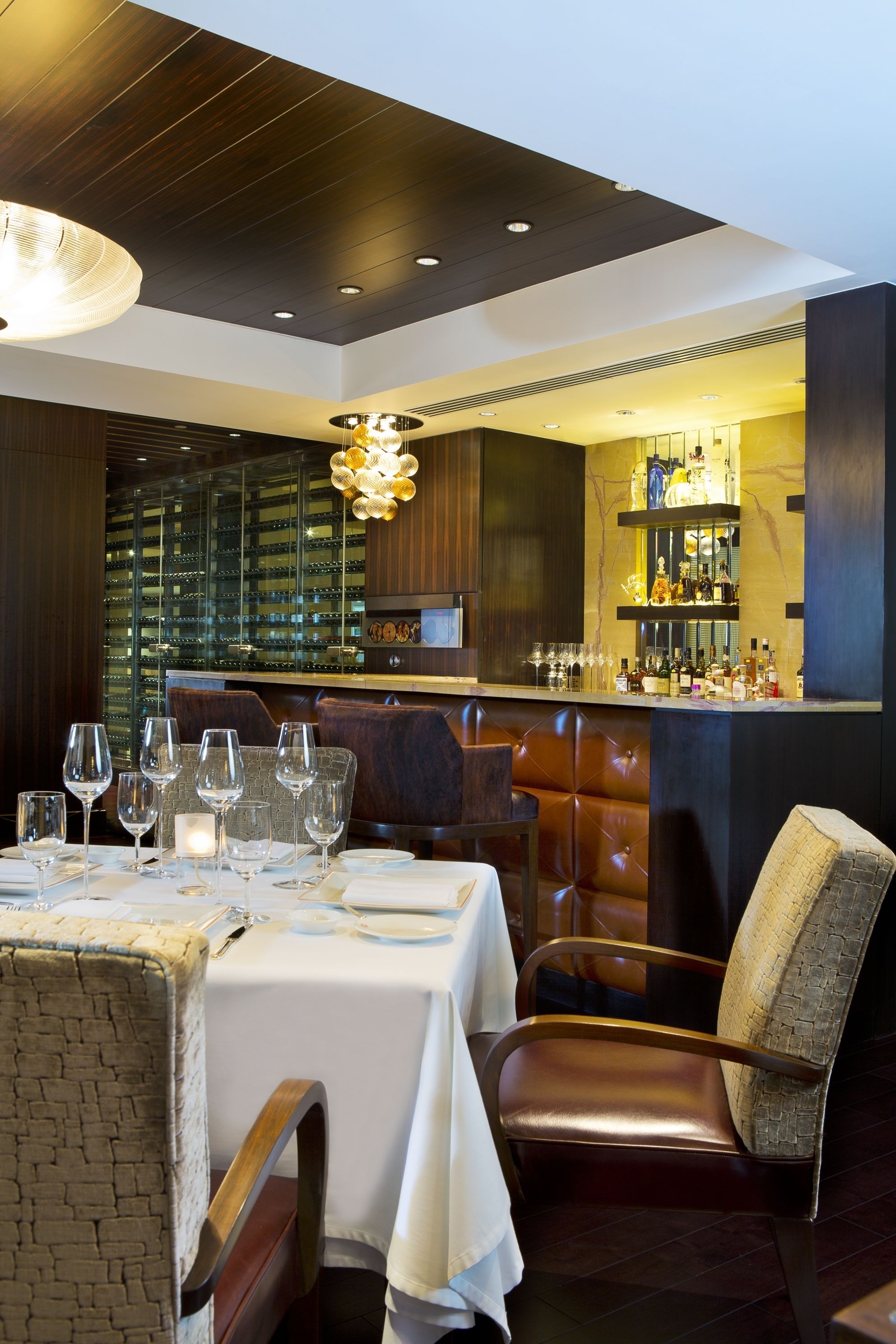 Um restaurante com área de bar, teto de madeira e disposição de mesas e cadeiras.