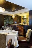 Um restaurante com área de bar, teto de madeira e disposição de mesas e cadeiras.