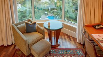 Quarto com sofá, uma mesa pequena e vista para uma piscina e vegetação através de janelas amplas.