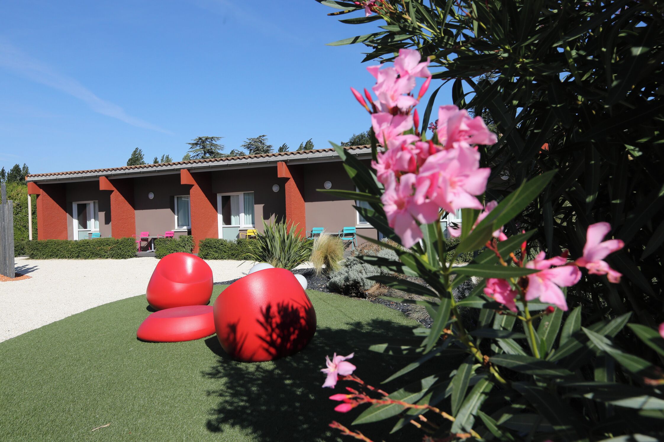 Um edifício com fachada em vermelho e bege, um gramado bem cuidado e esferas vermelhas.