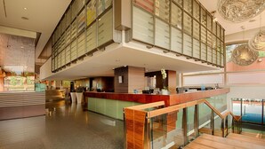 Um saguão moderno de hotel com balcão de recepção, escada e vista para o exterior.