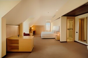 Quarto de hotel com escrivaninha, cama e área de estar.