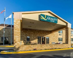 Edifício Quality Inn com fachada de tijolos, céu azul límpido e uma bandeira americana.