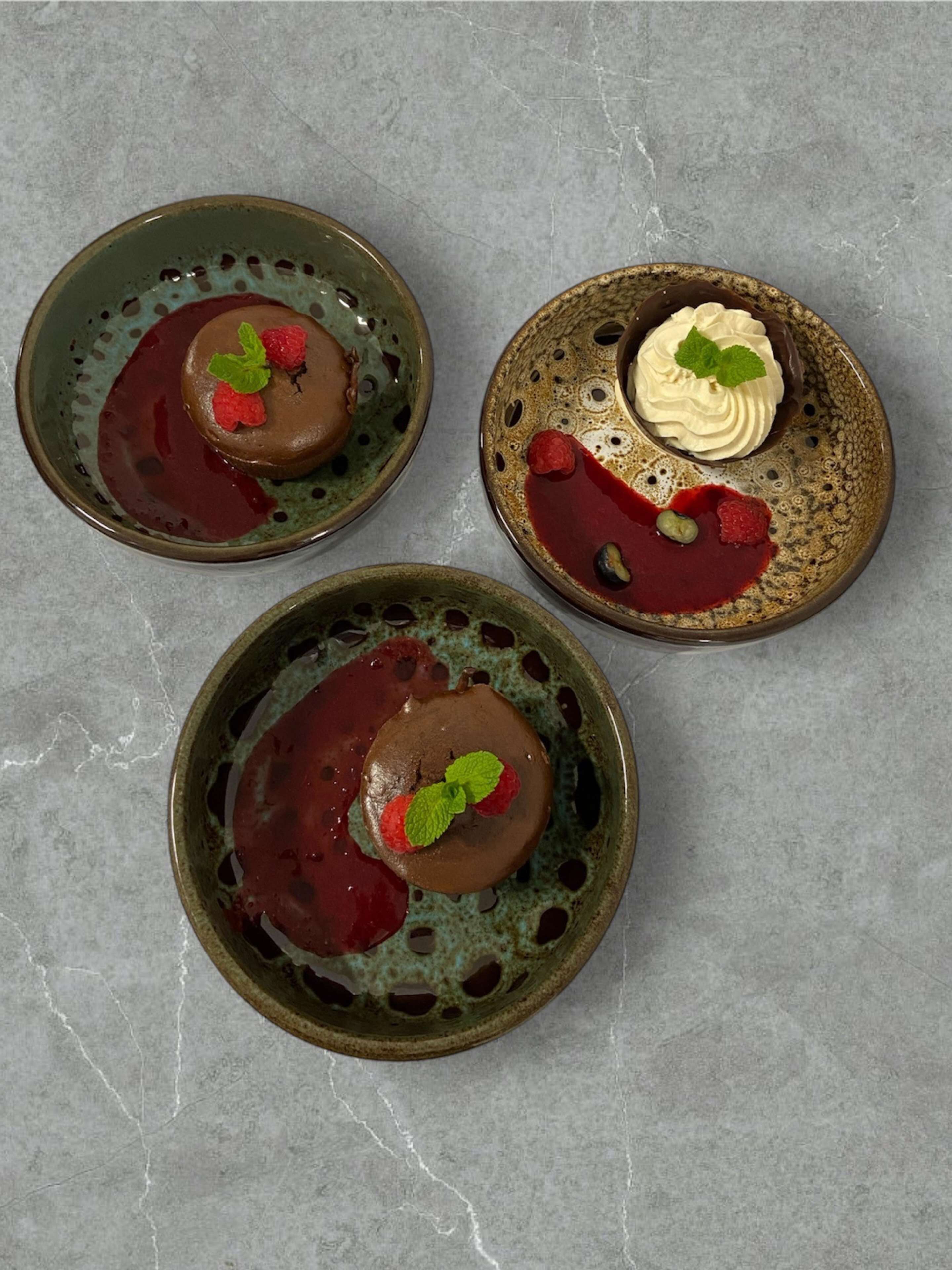 Três pratos de sobremesa com mousse de chocolate e frutas vermelhas sobre uma superfície texturizada.