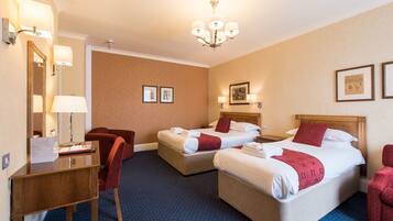 Quarto de hotel com duas camas, uma escrivaninha, uma cadeira e um candelabro.