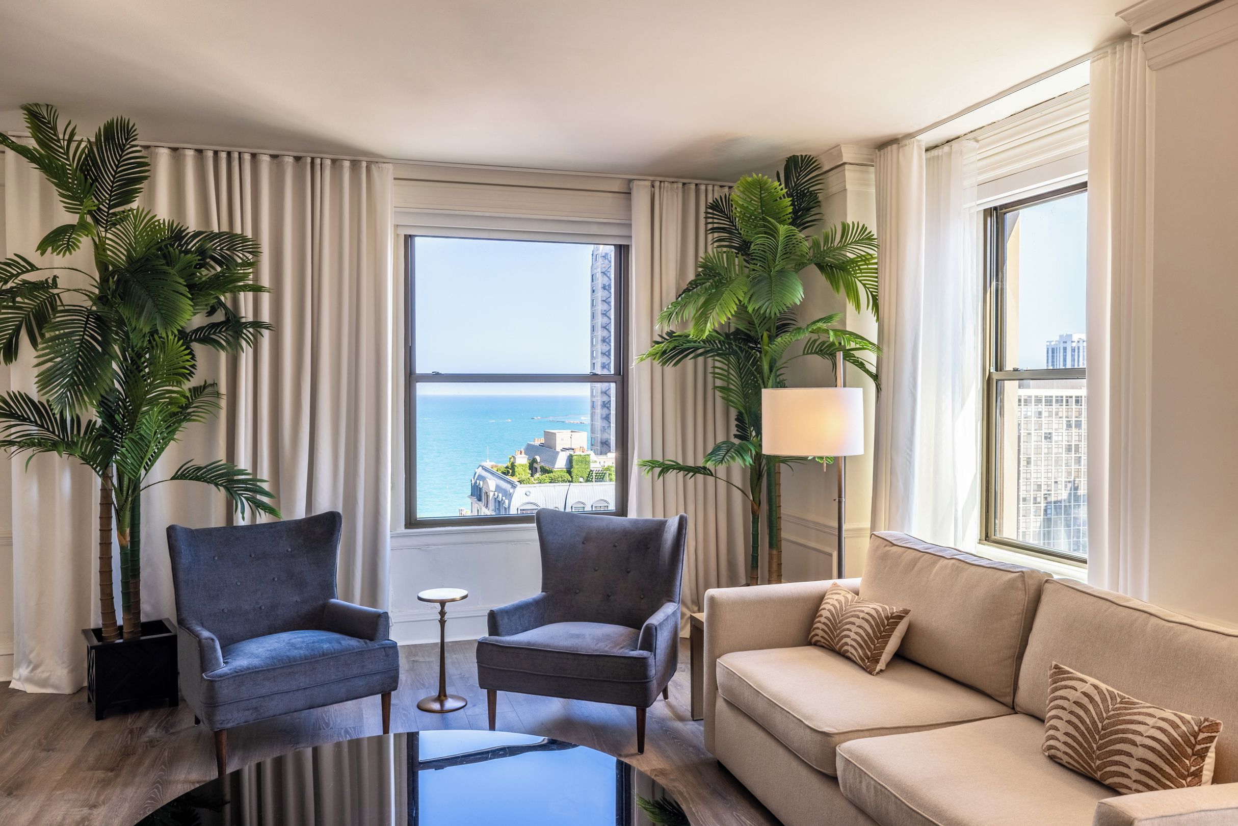 Sala de estar moderna com vista para o mar, dois poltronas, um sofá e uma mesa de centro.